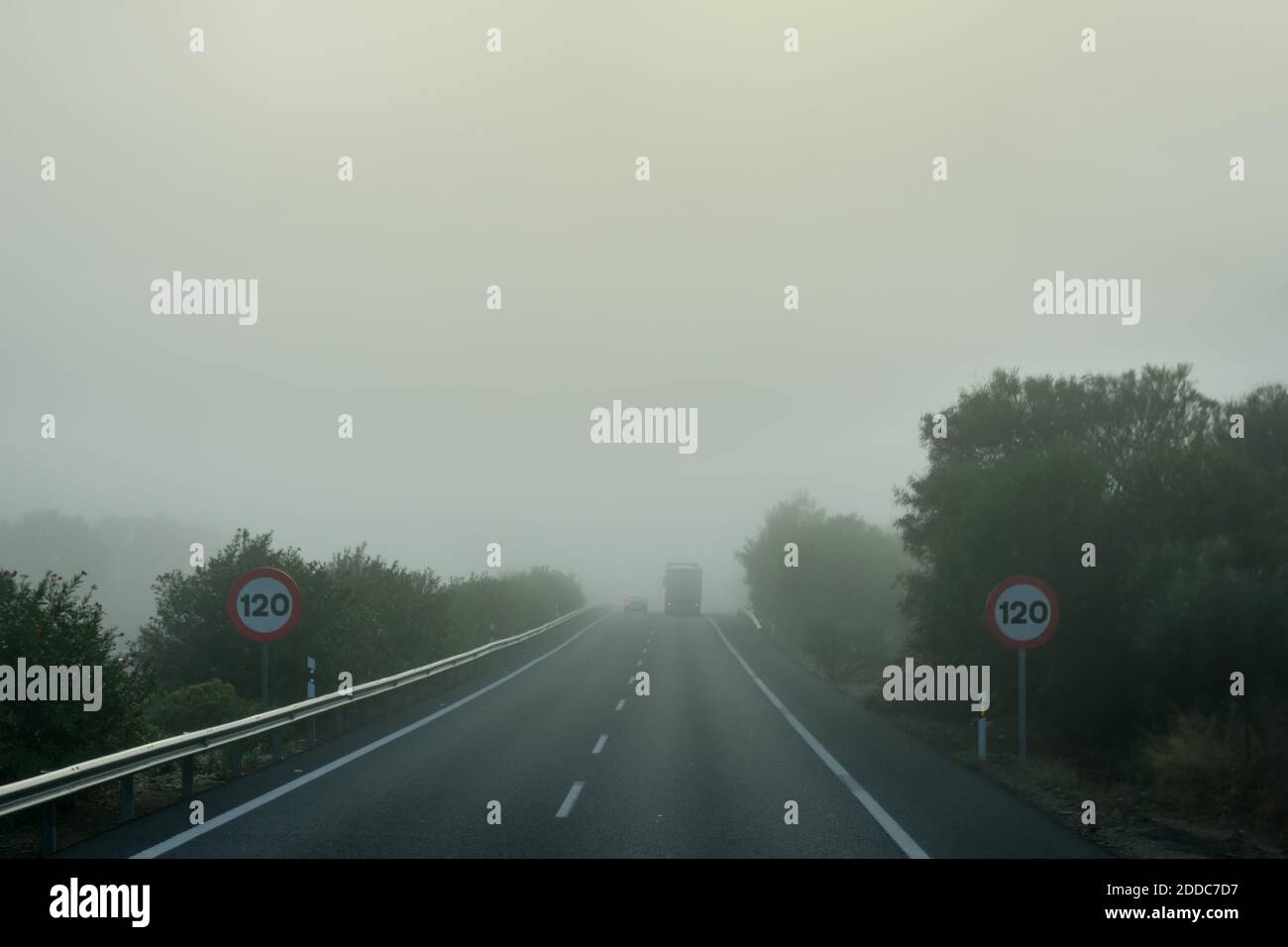 Straight of a highway with fog and two traffic signs indicating the ...