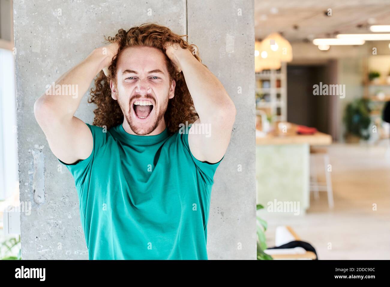 Angry man with hands in hair shouting while standing against column in ...