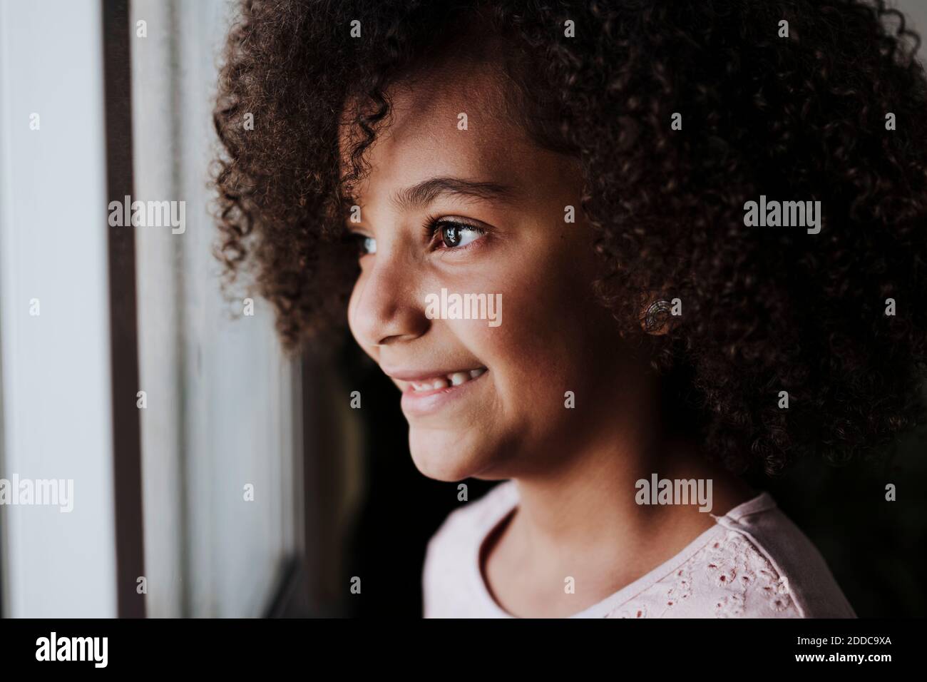 Smiling girl looking through window at home Stock Photo - Alamy