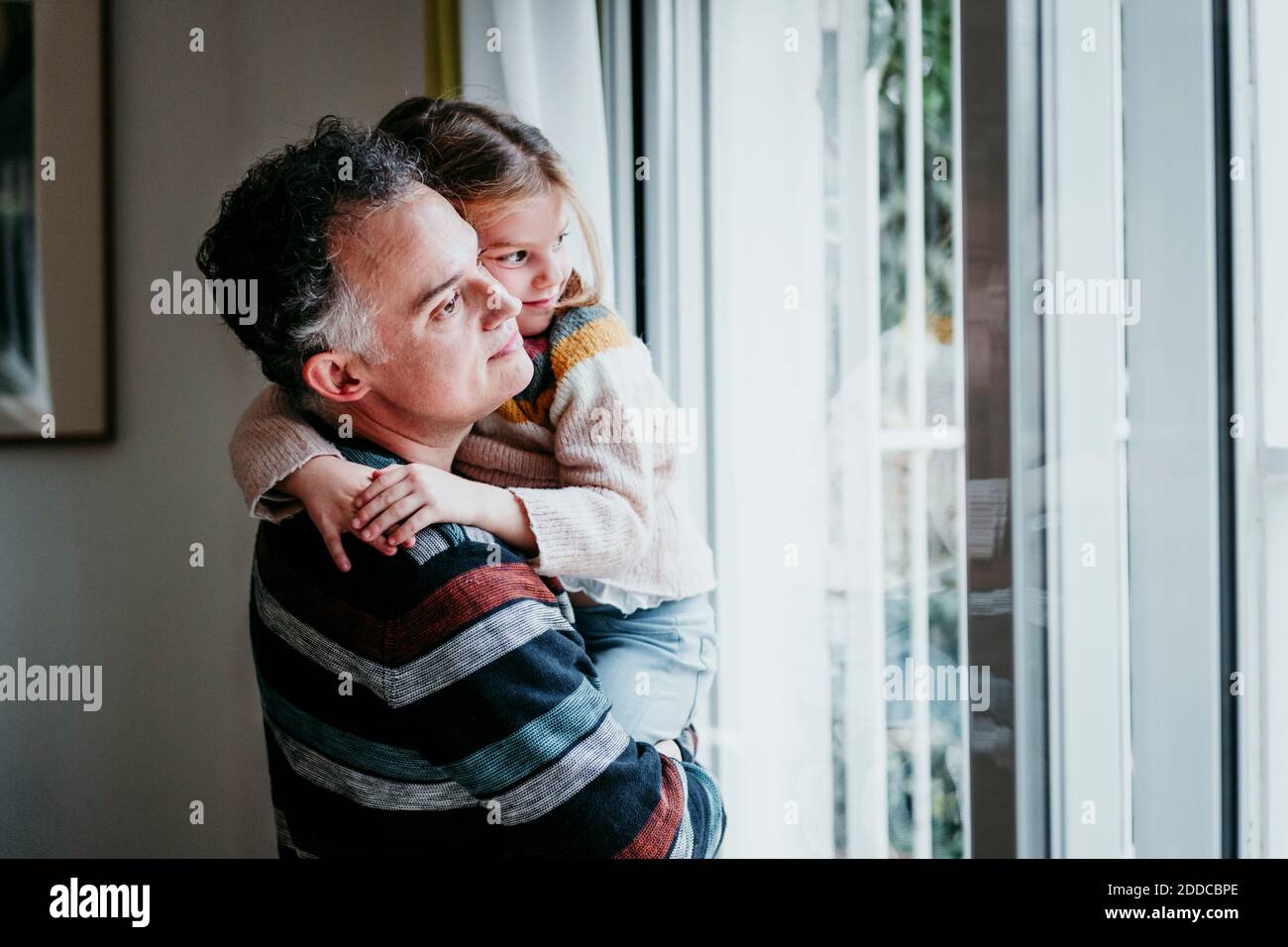 Father carrying daughter while standing by window at home Stock Photo ...