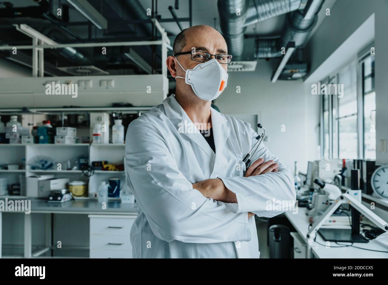Confident scientist wearing face mask standing with arms crossed at ...