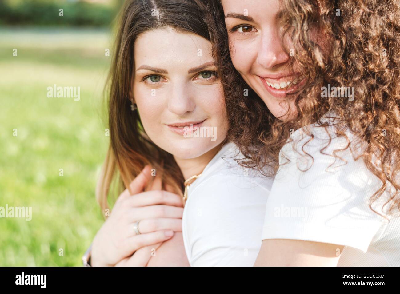 Happy young woman hugging beautiful female friend from behind at park ...
