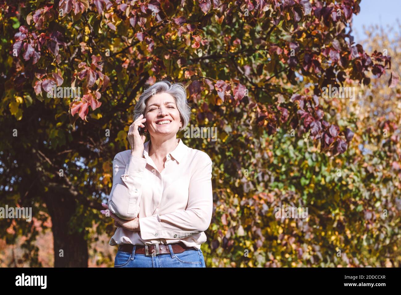 Smiling mature woman talking on mobile phone while standing against ...