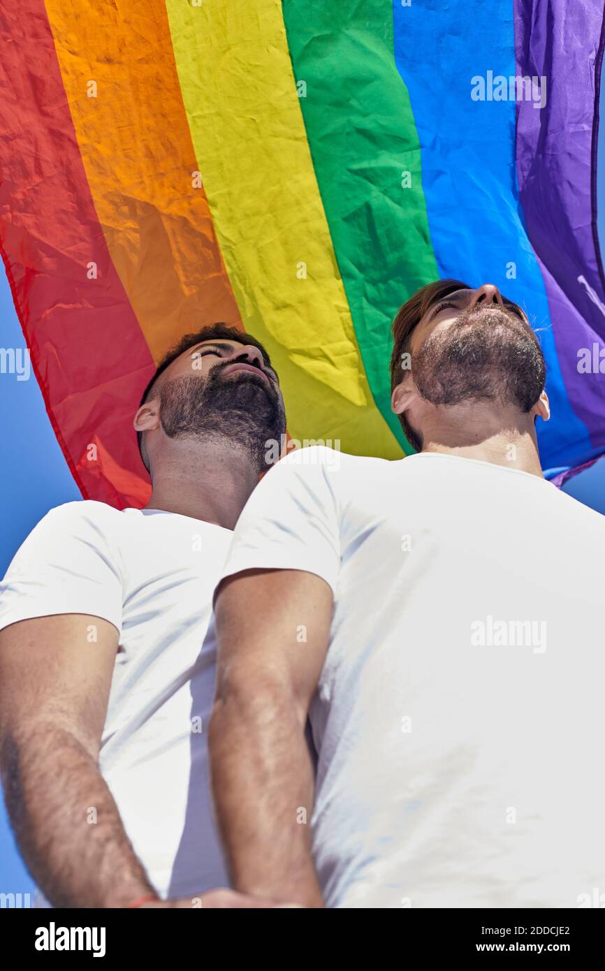 Gay couple looking away while standing under rainbow flag Stock Photo ...