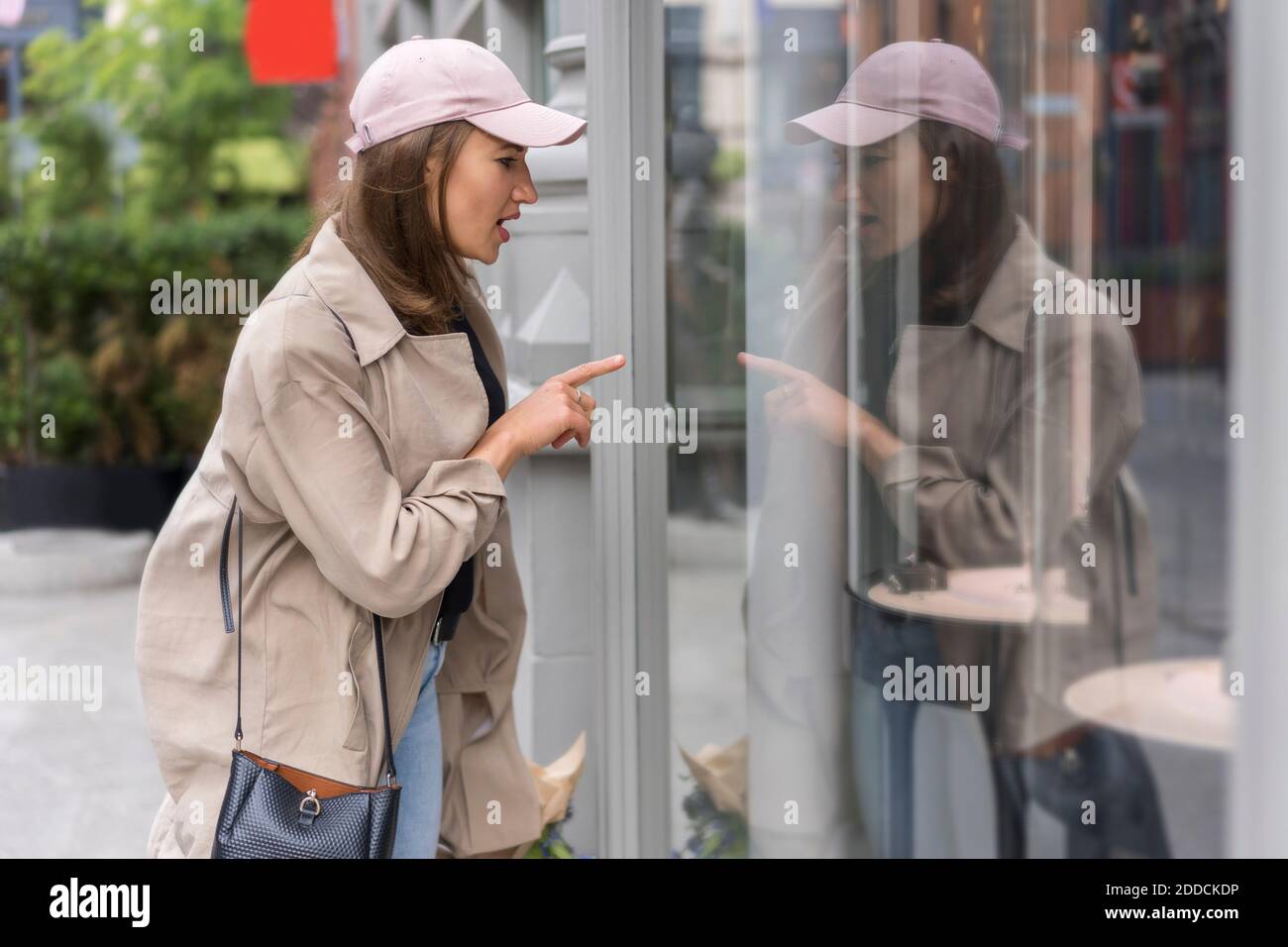Woman wearing cap pointing at reflection on glass door in city Stock ...