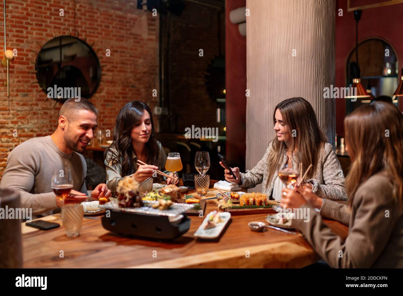 Woman using mobile phone while sitting by friends eating food at ...