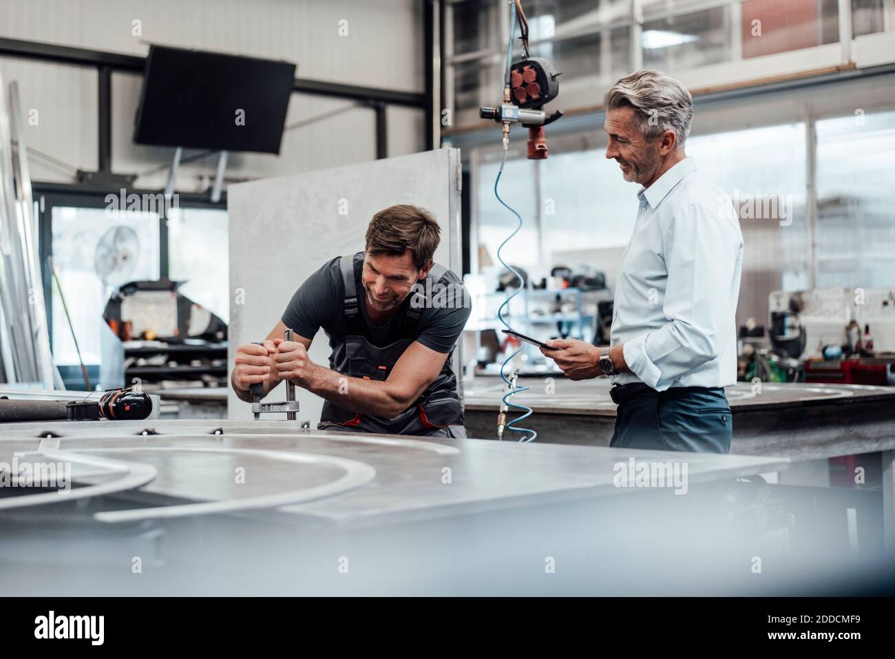 Male manager discussing with worker operating manufacturing equipment ...