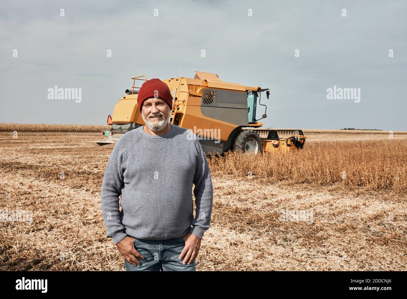 Smiling farmer standing against tractor harvesting crop at farm Stock ...