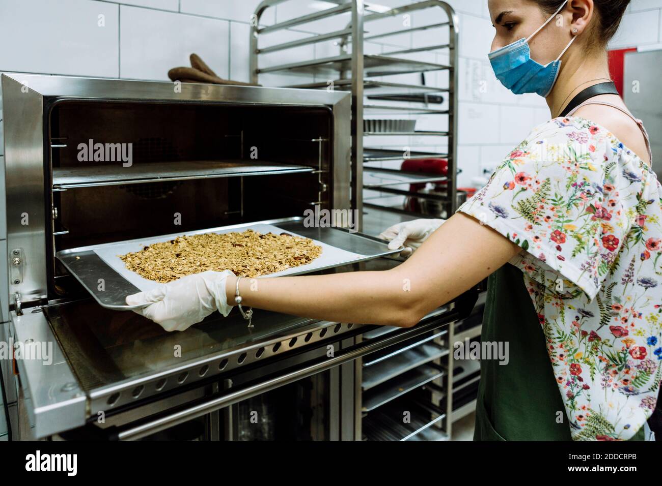 Young female baker positioning sheet in oven at bakery kitchen during ...