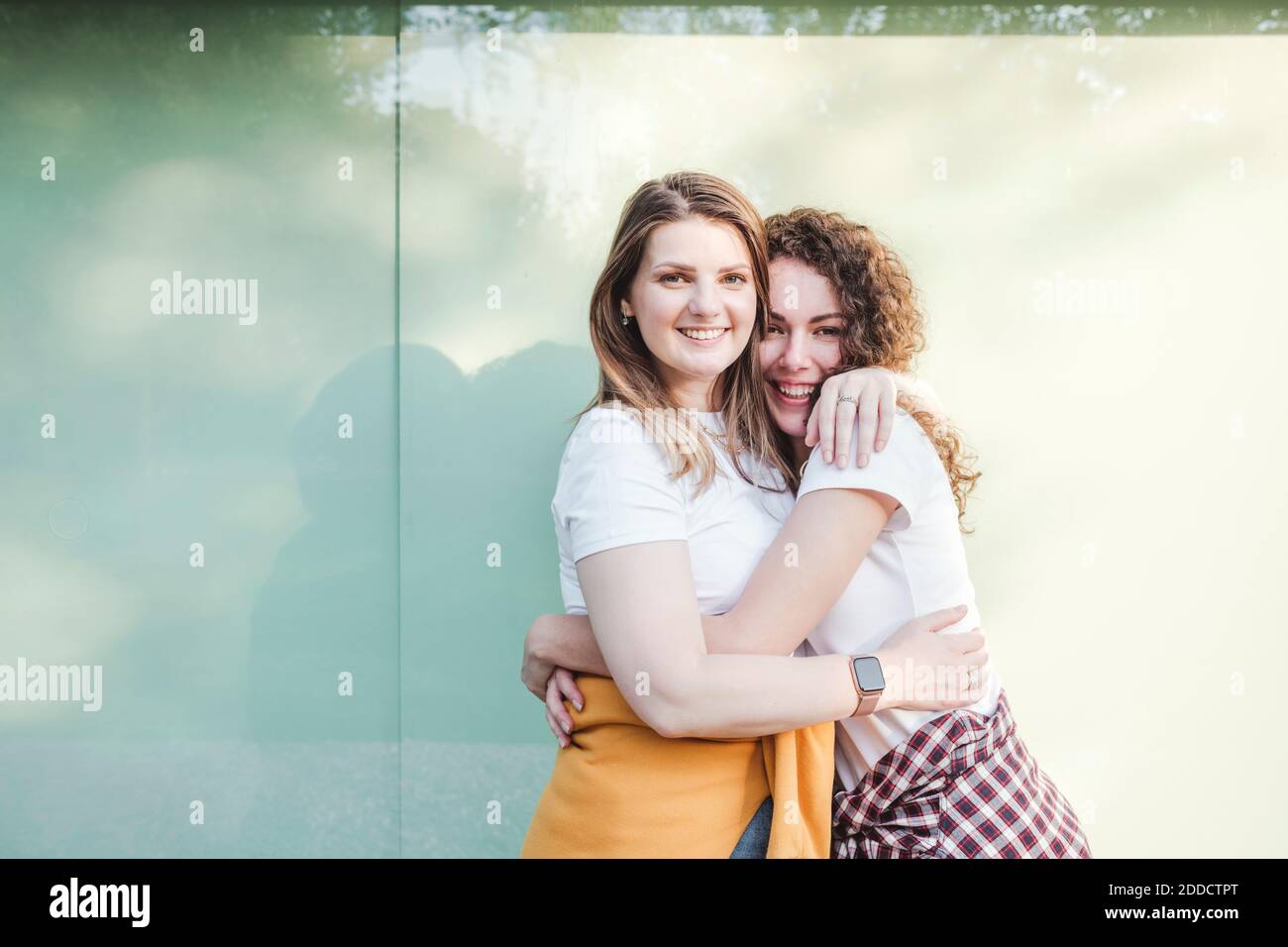 Smiling beautiful women hugging each other against wall Stock Photo - Alamy