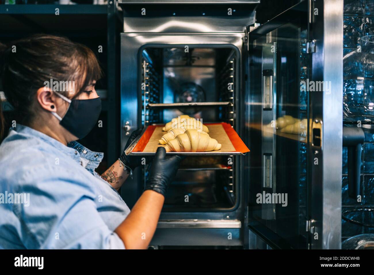 Female chef putting baking sheet with croissants in oven at restaurant ...