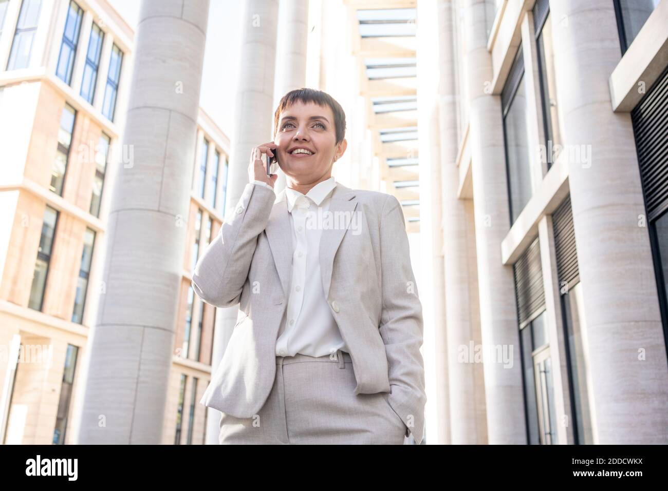 Woman talking on mobile phone while standing against office building ...