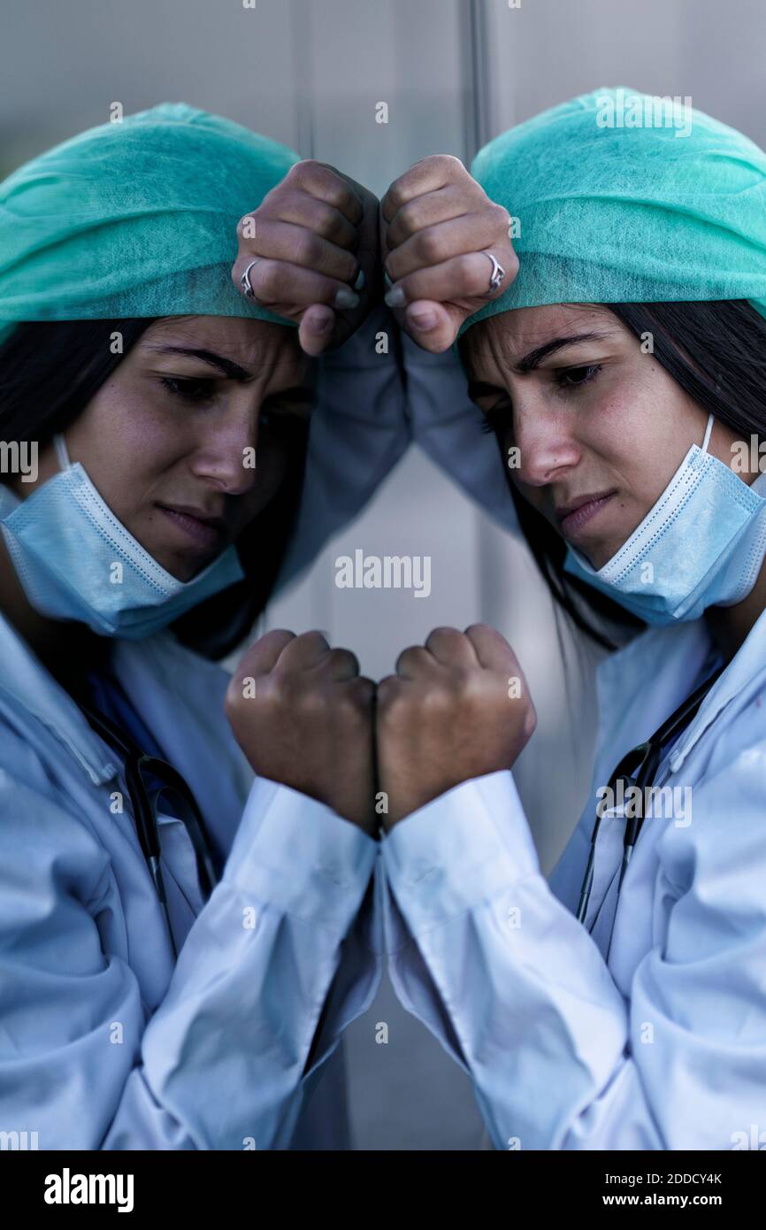 Sad doctor wearing face mask leaning on glass wall of hospital Stock ...