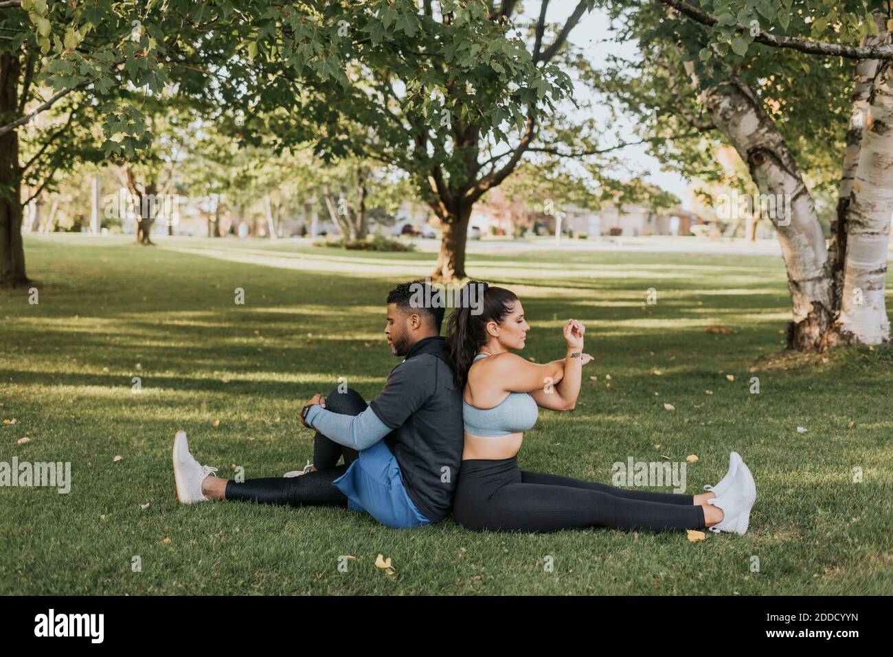 Couple stretching while sitting back to back at backyard Stock Photo ...