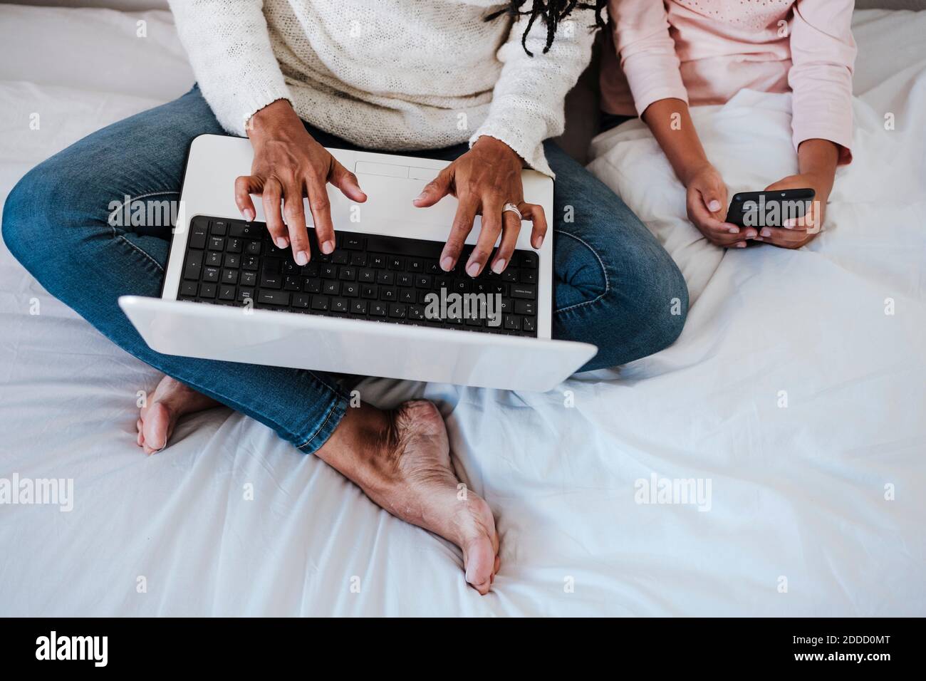 Low section of mother using laptop sitting with daughter text messaging ...