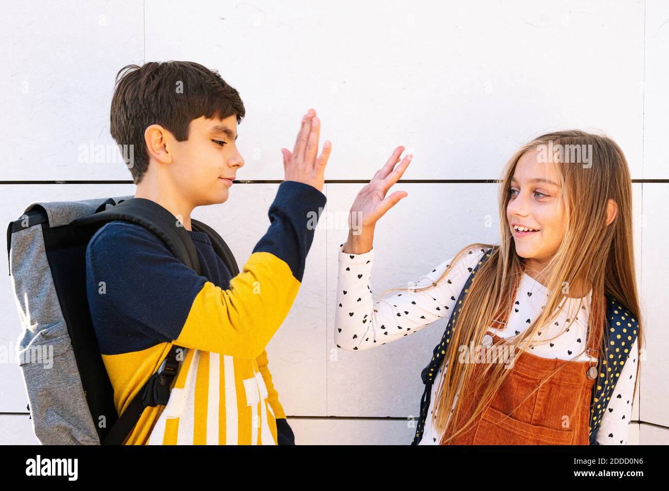 Brother and sister doing high five while standing against white wall on ...