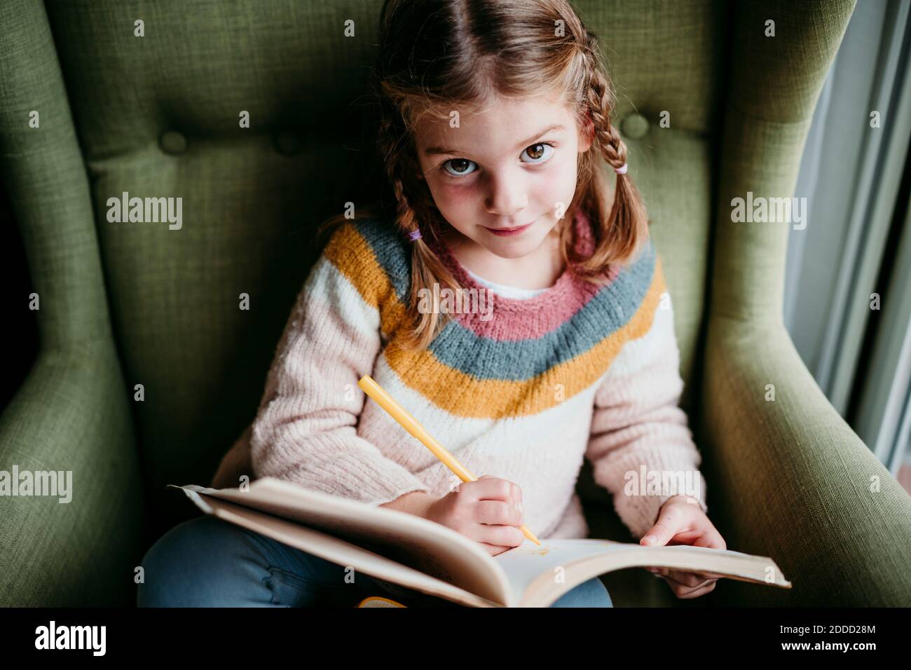 Cute girl doing homework while sitting on chair at home Stock Photo - Alamy