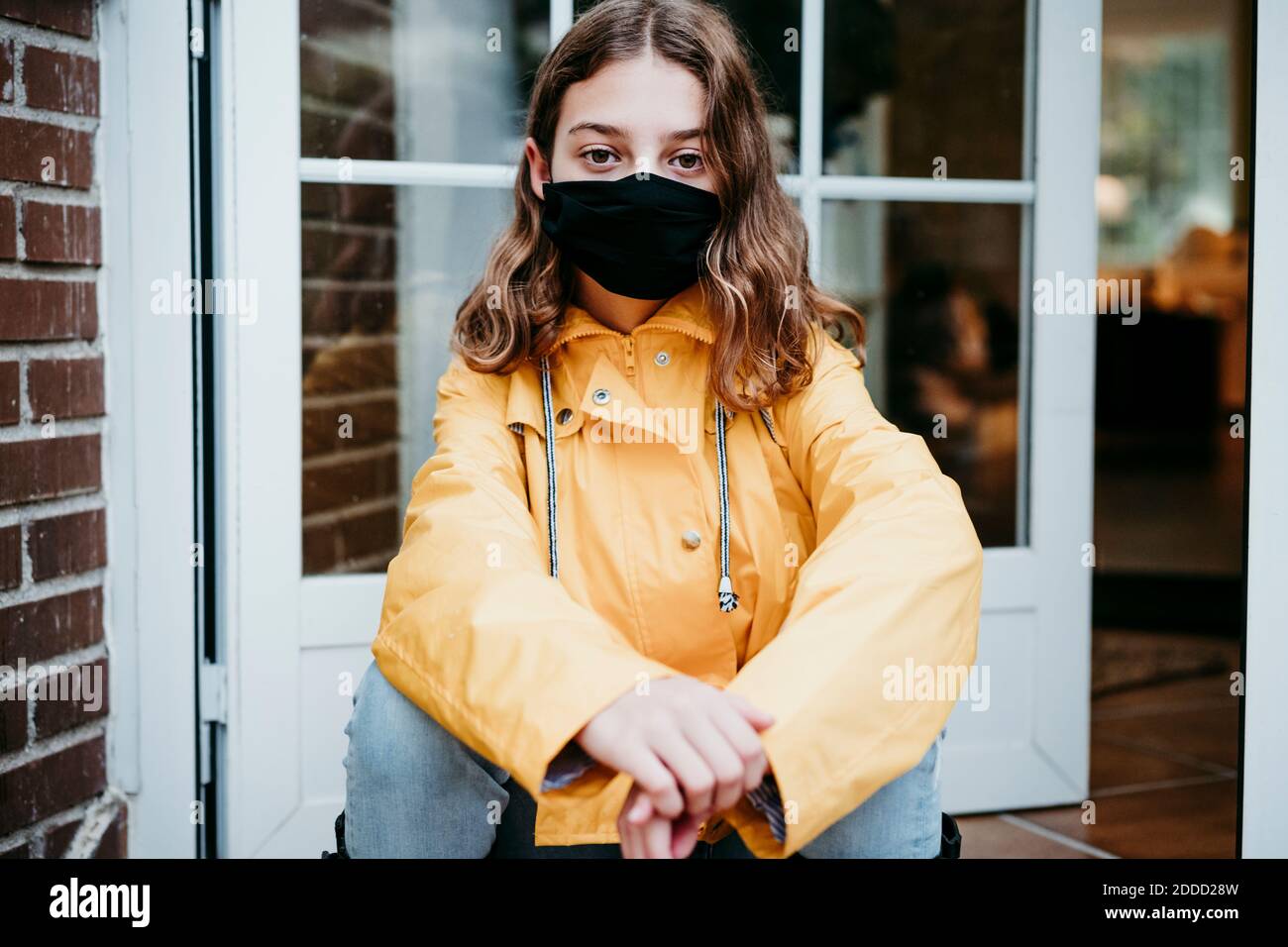 Girl wearing protective face mask sitting on floor against door Stock ...