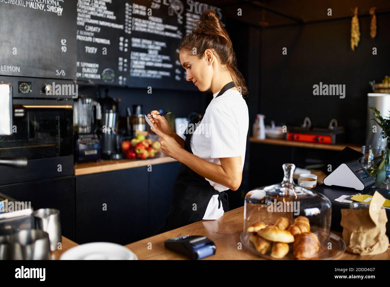 Barista writing in note pad while working at coffee shop Stock Photo ...