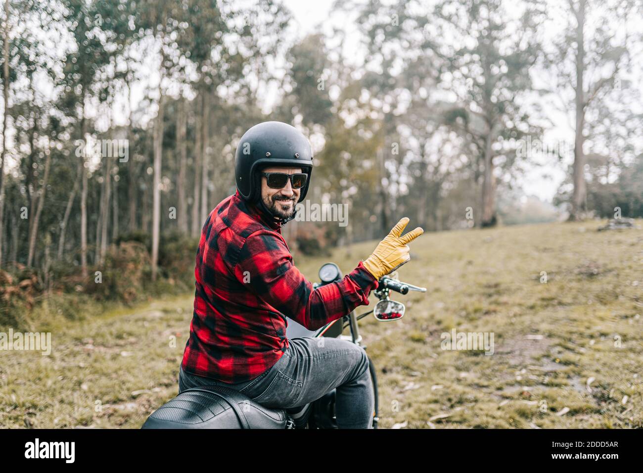Smiling male biker gesturing while exploring forest on motorcycle Stock ...