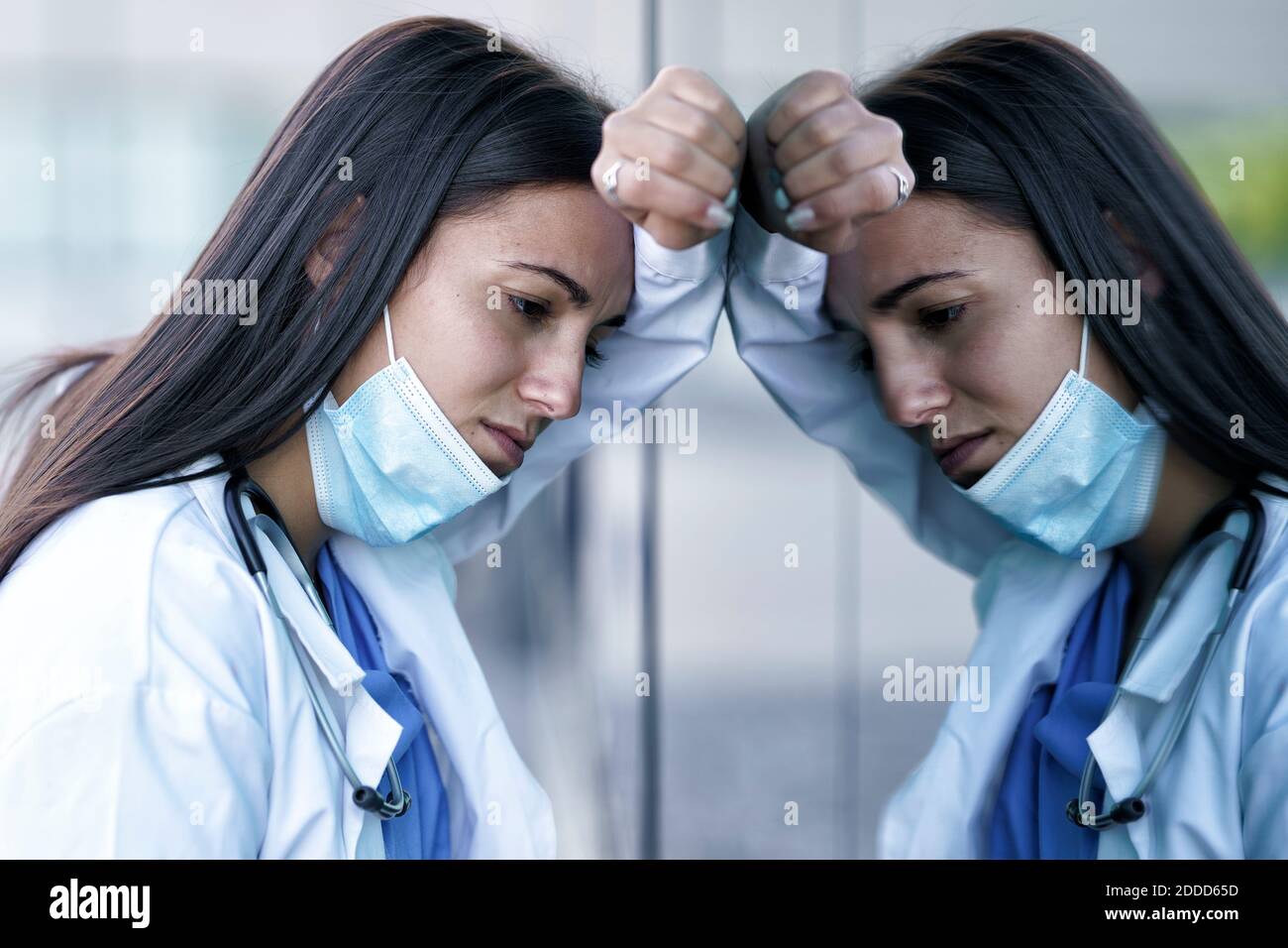 Tired doctor wearing face mask leaning on glass wall of hospital Stock ...