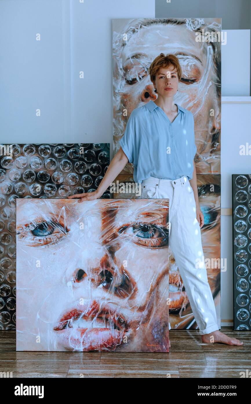 Confident mid adult female artist standing with various paintings in ...