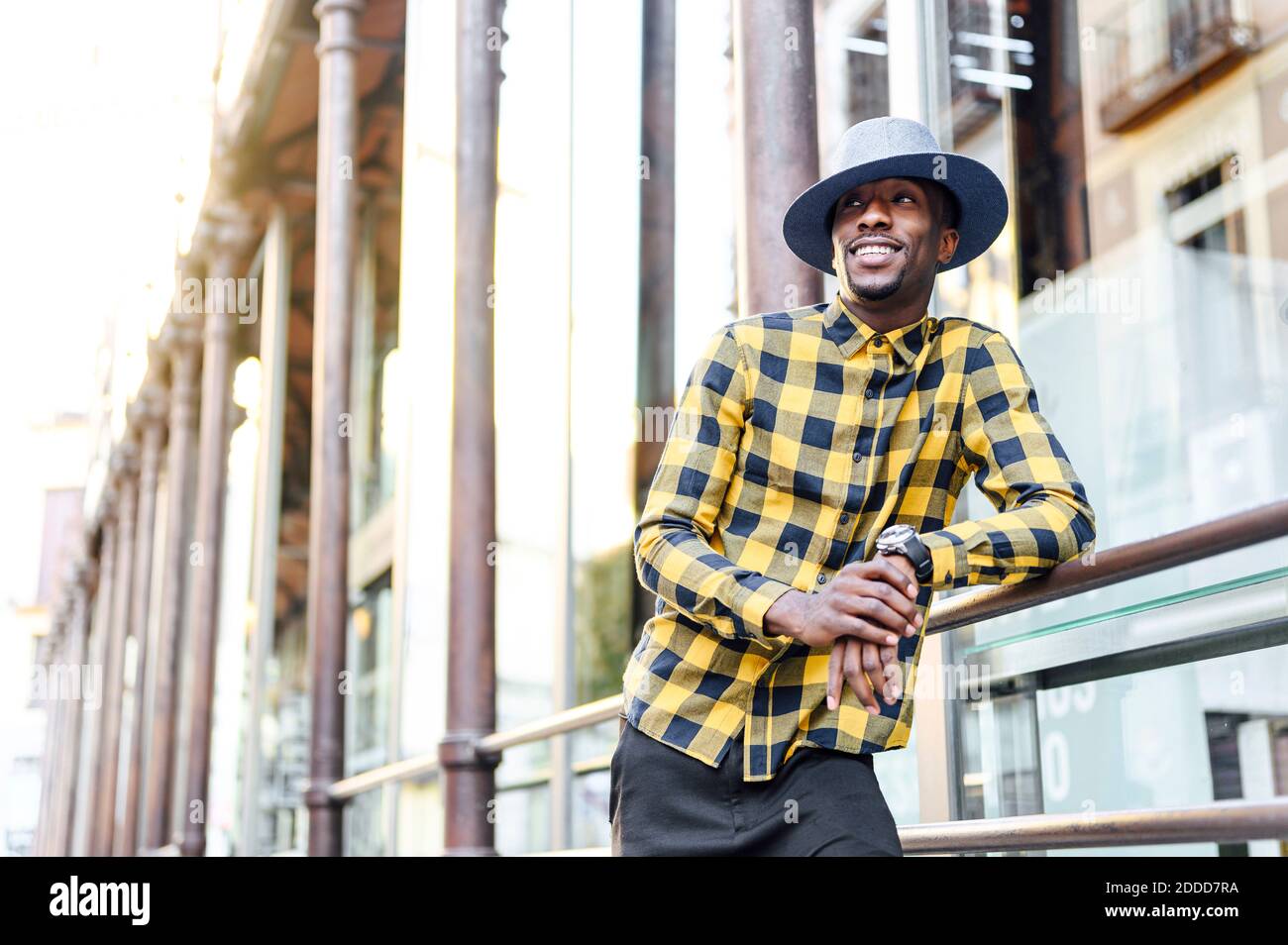 Smiling african man looking away while leaning over building railing ...