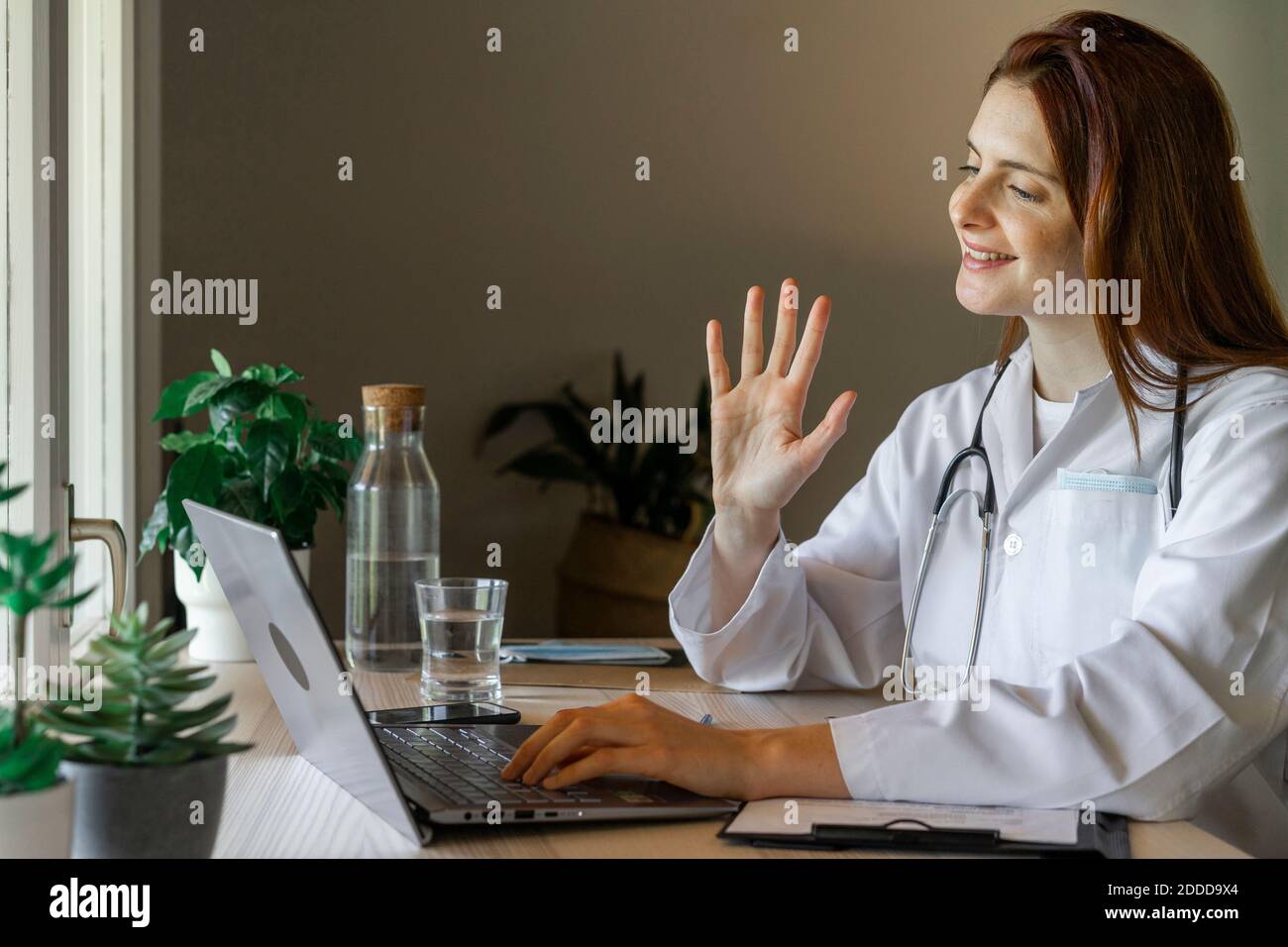 Young female doctor waving hand at patient while providing online ...