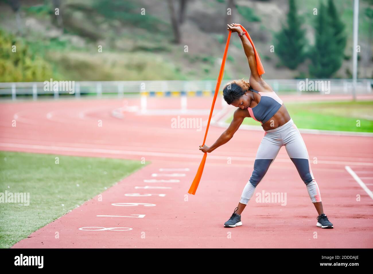 Female athlete stretching resistance band while standing on running ...