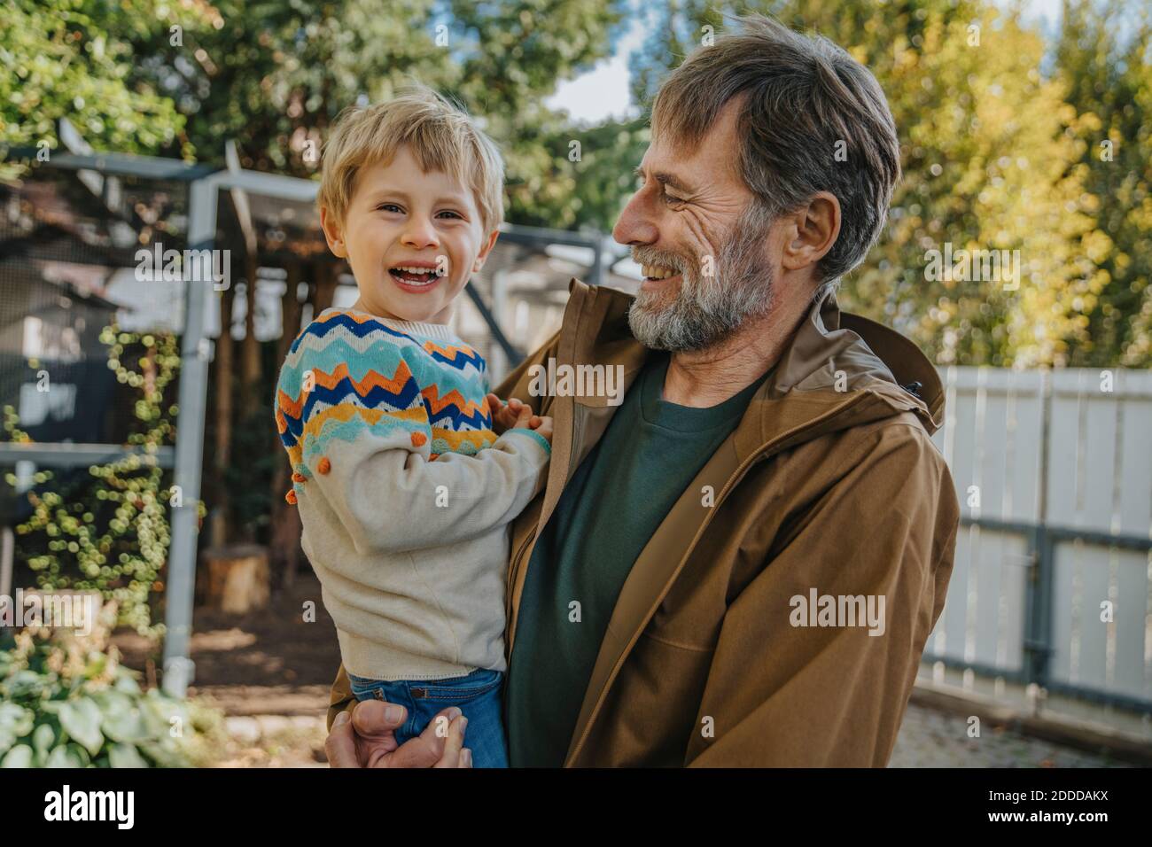 Father laughing while carrying son standing in back yard on sunny day ...