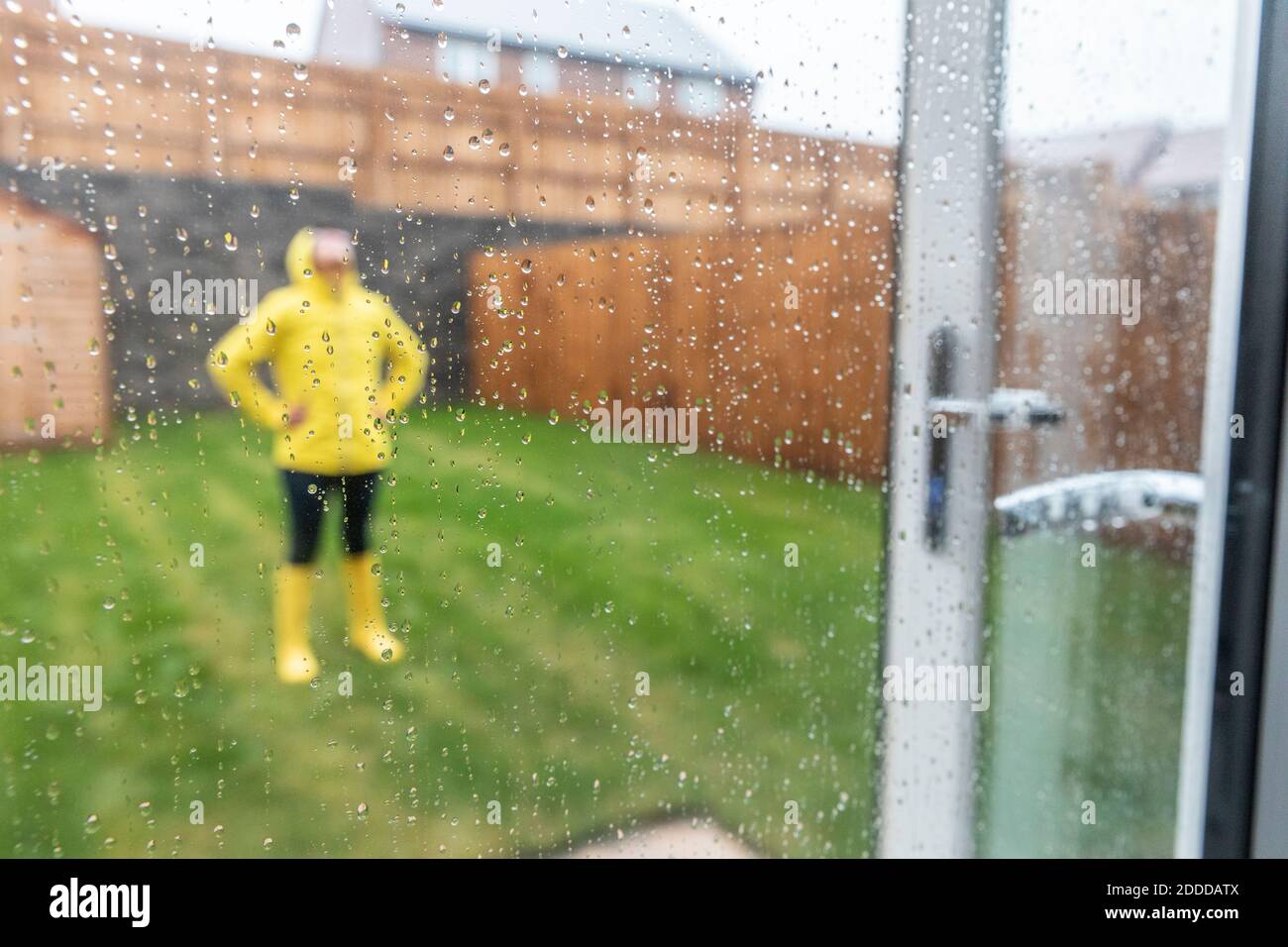 Woman enjoying rain with hand on hip while standing in back yard during ...