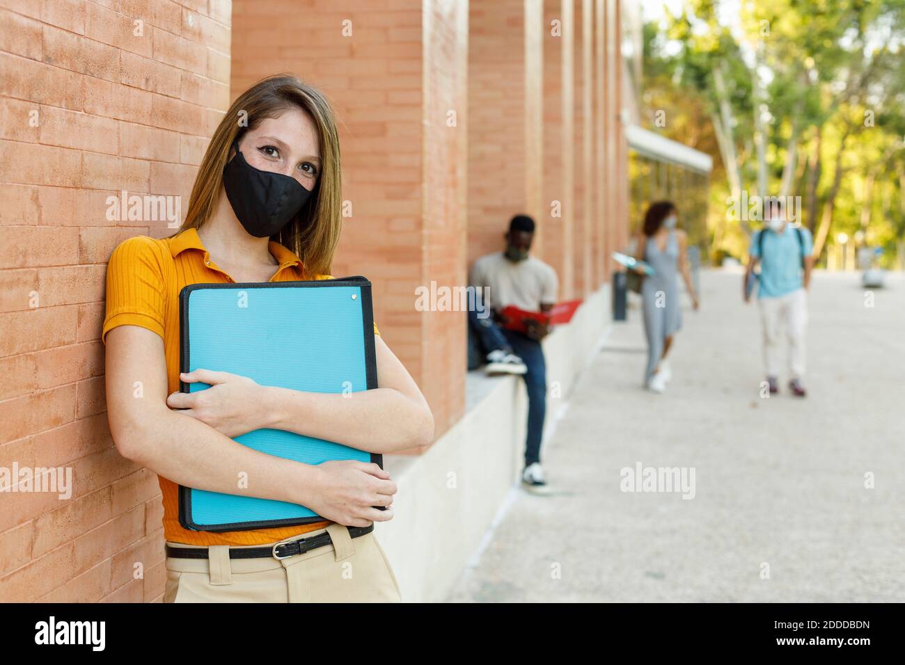 Young woman with folder wearing protective face mask while standing in ...