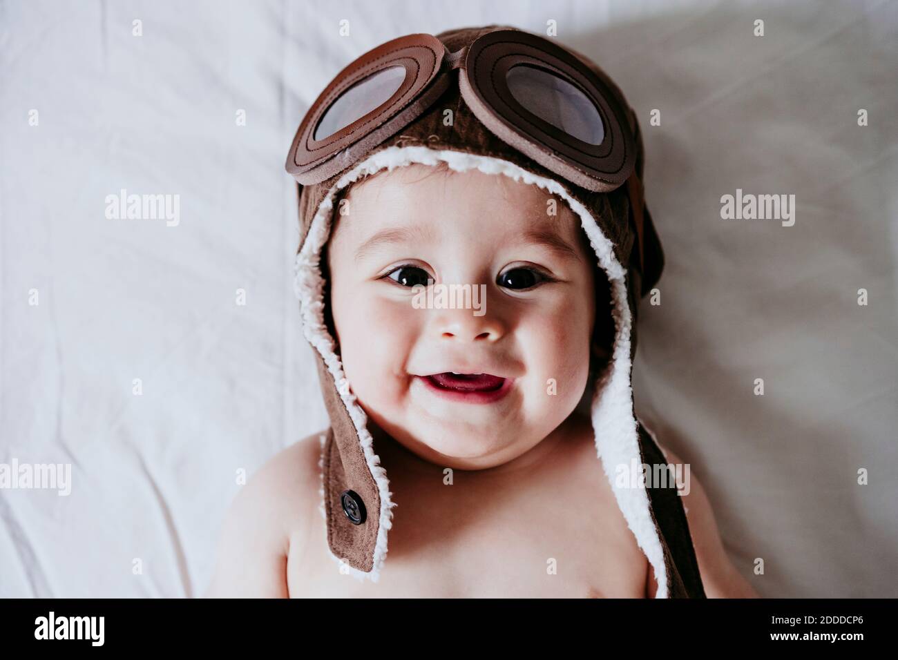 Cute male toddle wearing aviator cap while lying down on bed at home ...
