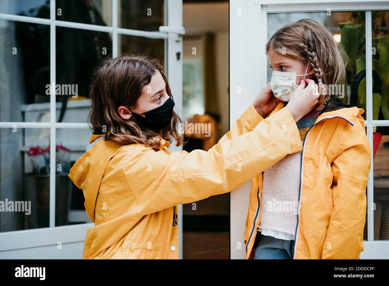 Sister adjusting face mask of sister while sitting against door Stock ...