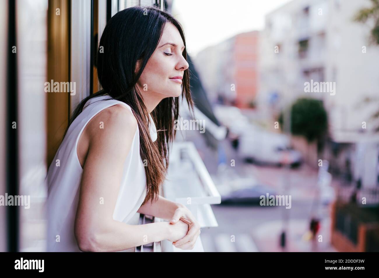Mid adult woman leaning out of window with eyes closed while standing ...