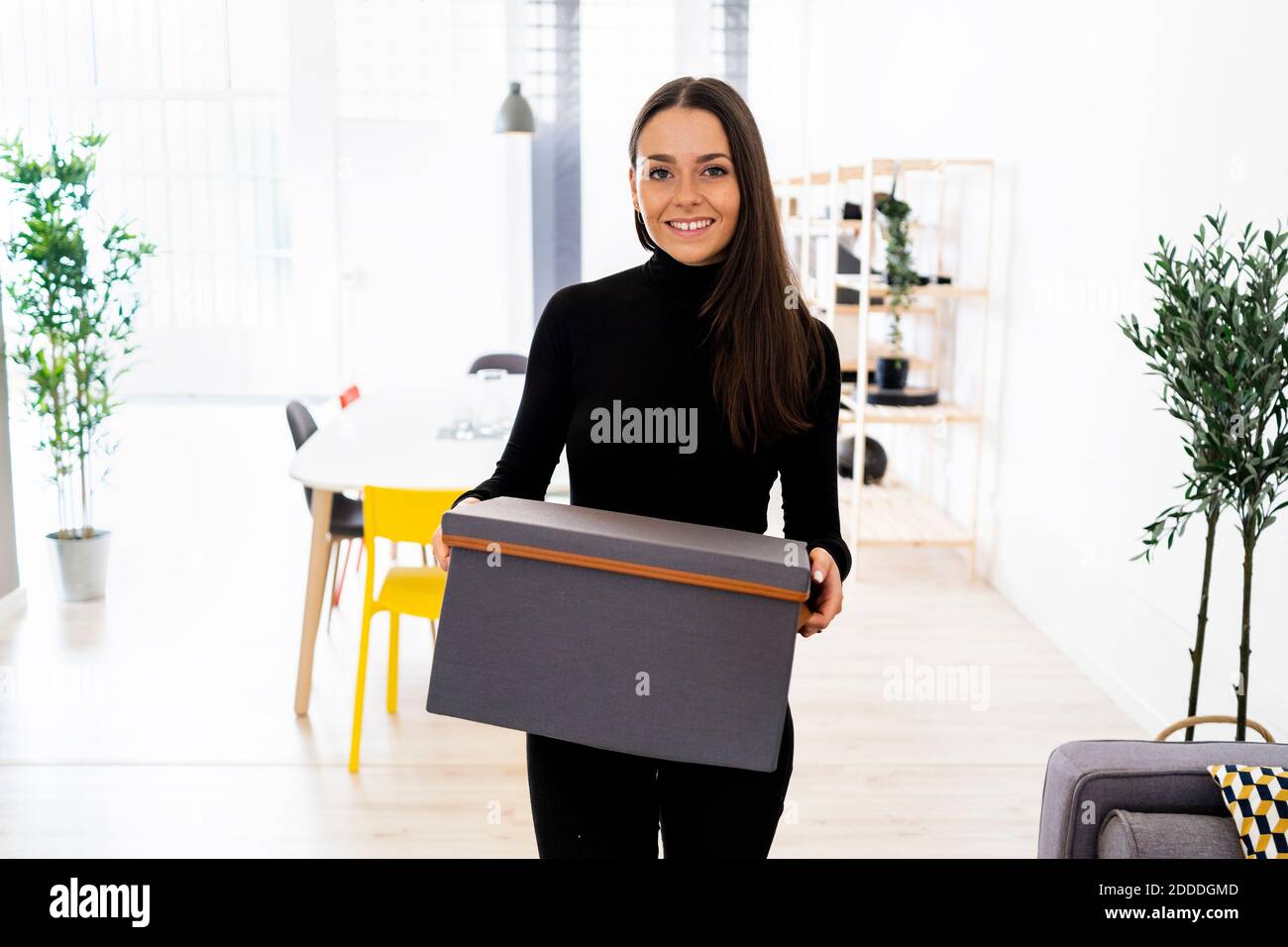 Smiling beautiful young woman carrying box at loft apartment Stock ...