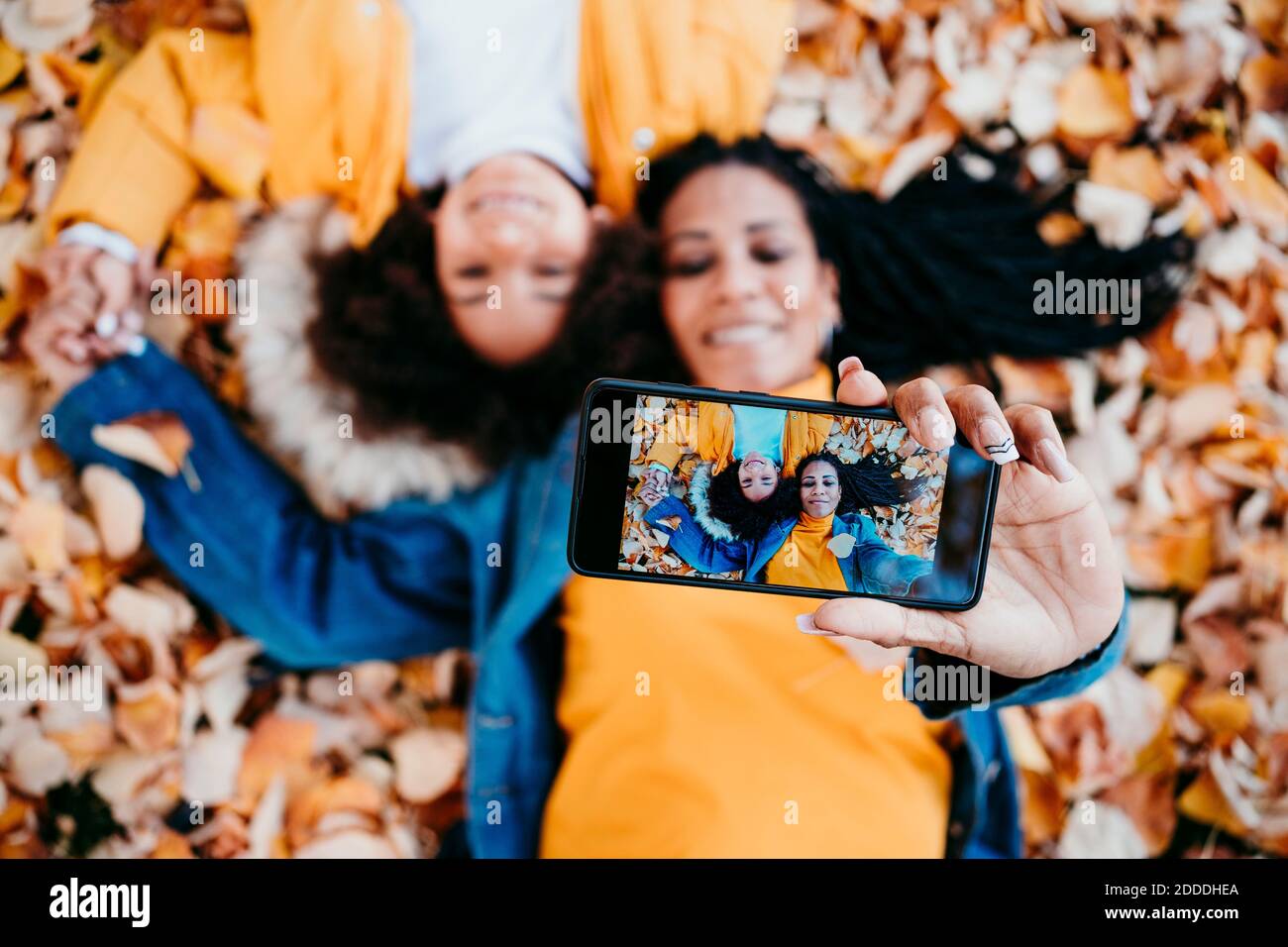 Woman taking photo with daughter through mobile phone while lying on ...