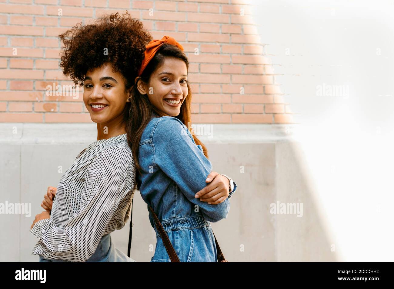 Smiling friends standing back to back against wall Stock Photo - Alamy