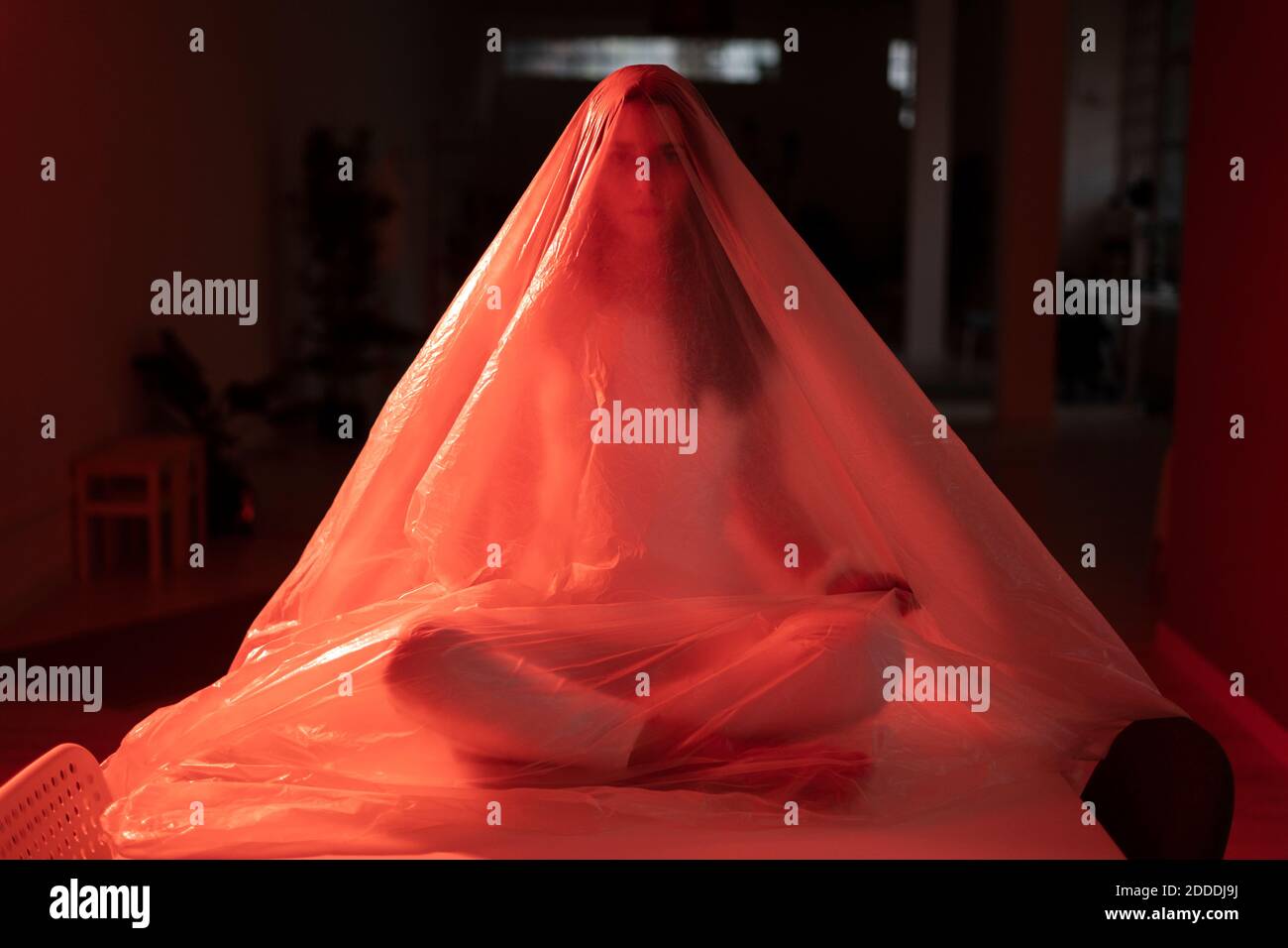Young woman covered in plastic sitting with cross-legged on table ...