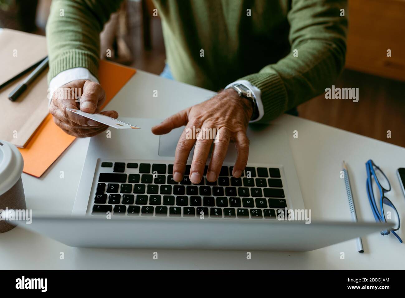 Midsection of man using credit card while working on laptop at home ...
