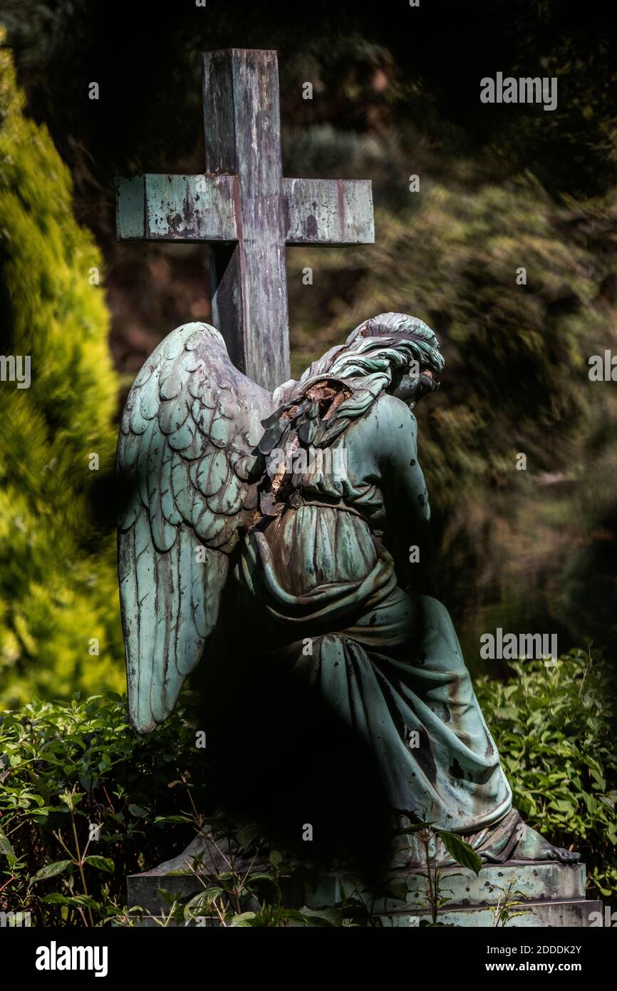 Weathered statue of angel sitting beside cross in cemetery Stock Photo ...