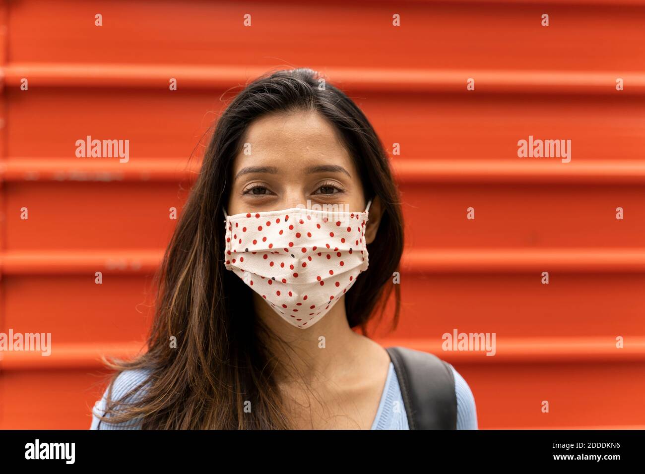 Contemplating woman with protective face mask standing against shutter ...