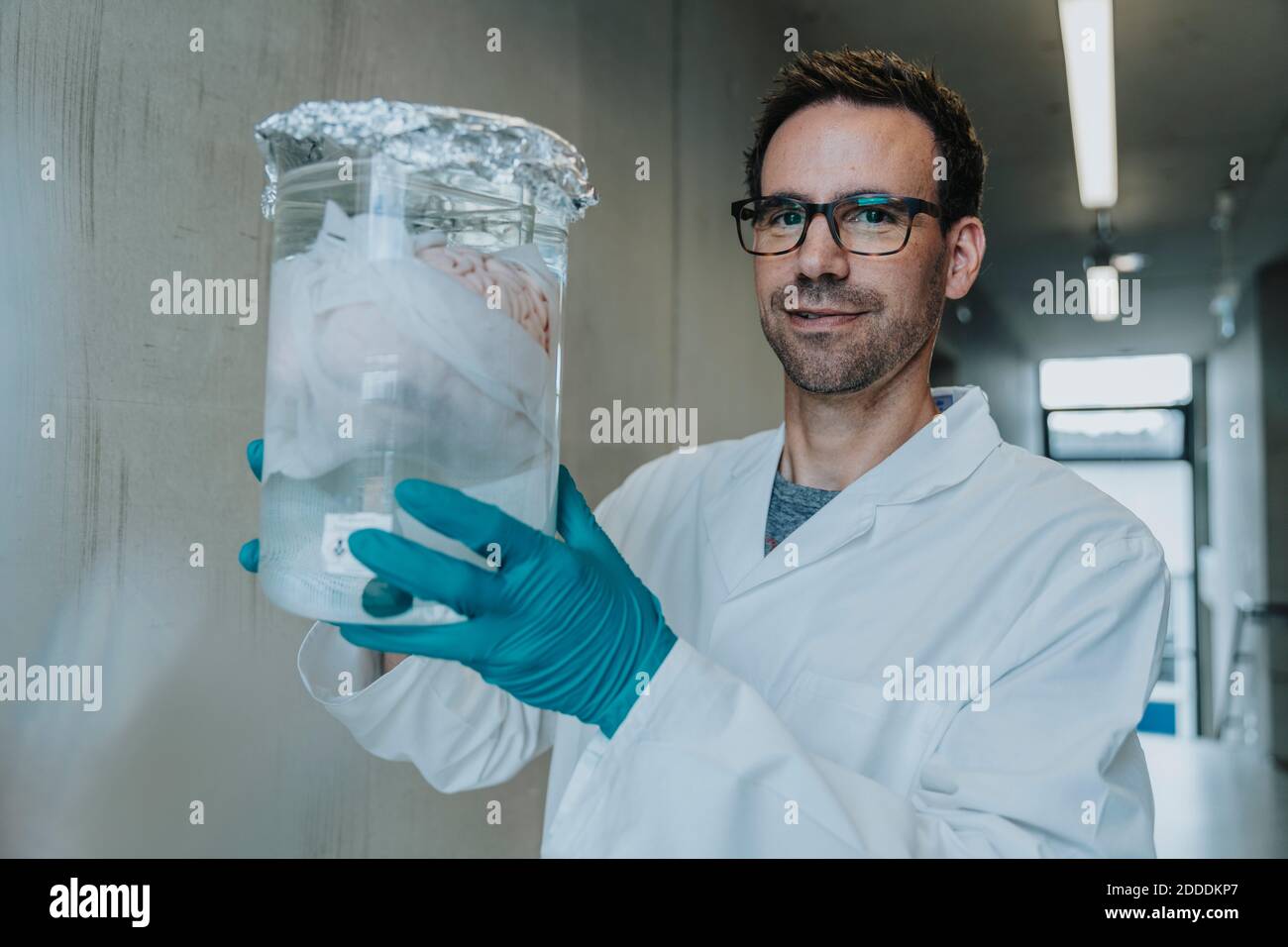Scientist holding preserved human brain beaker while standing at clinic ...