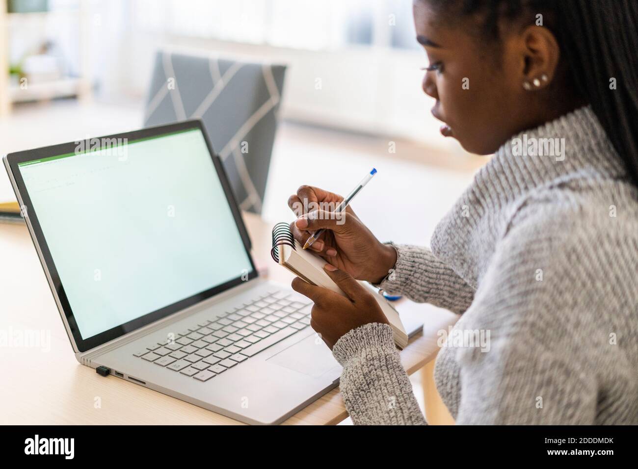 Young woman writing in notepad while studying through laptop at home ...