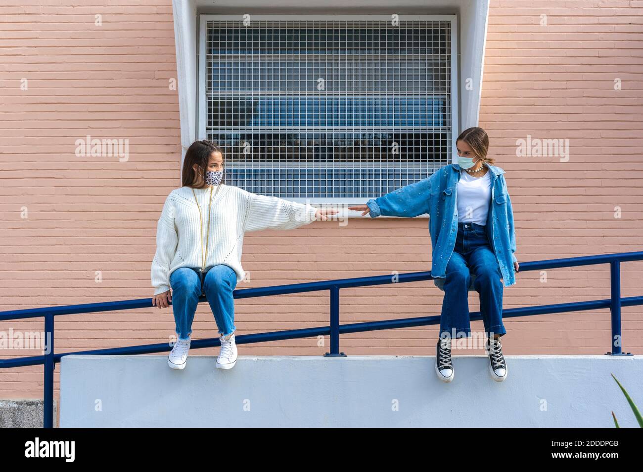 Teenage friends social distancing while sitting on railing during covid ...