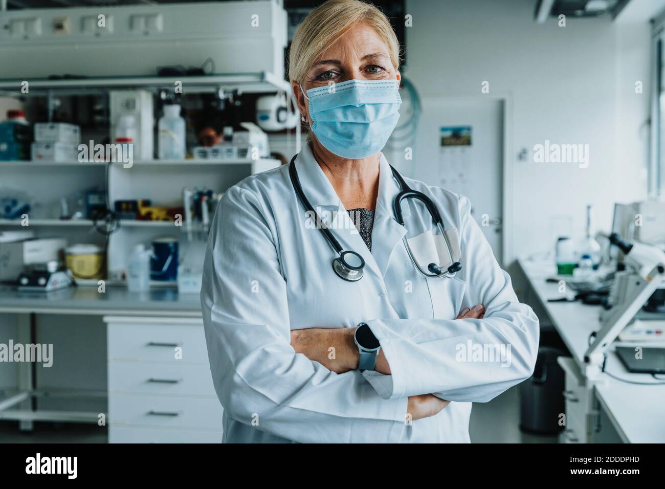 Confident scientist wearing face mask standing with arms crossed at ...
