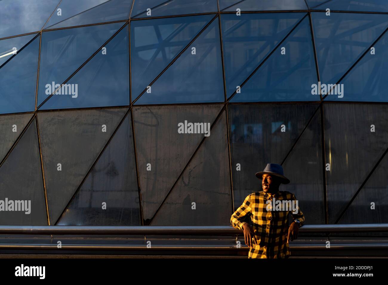 Smiling african man looking away while standing against glass building ...