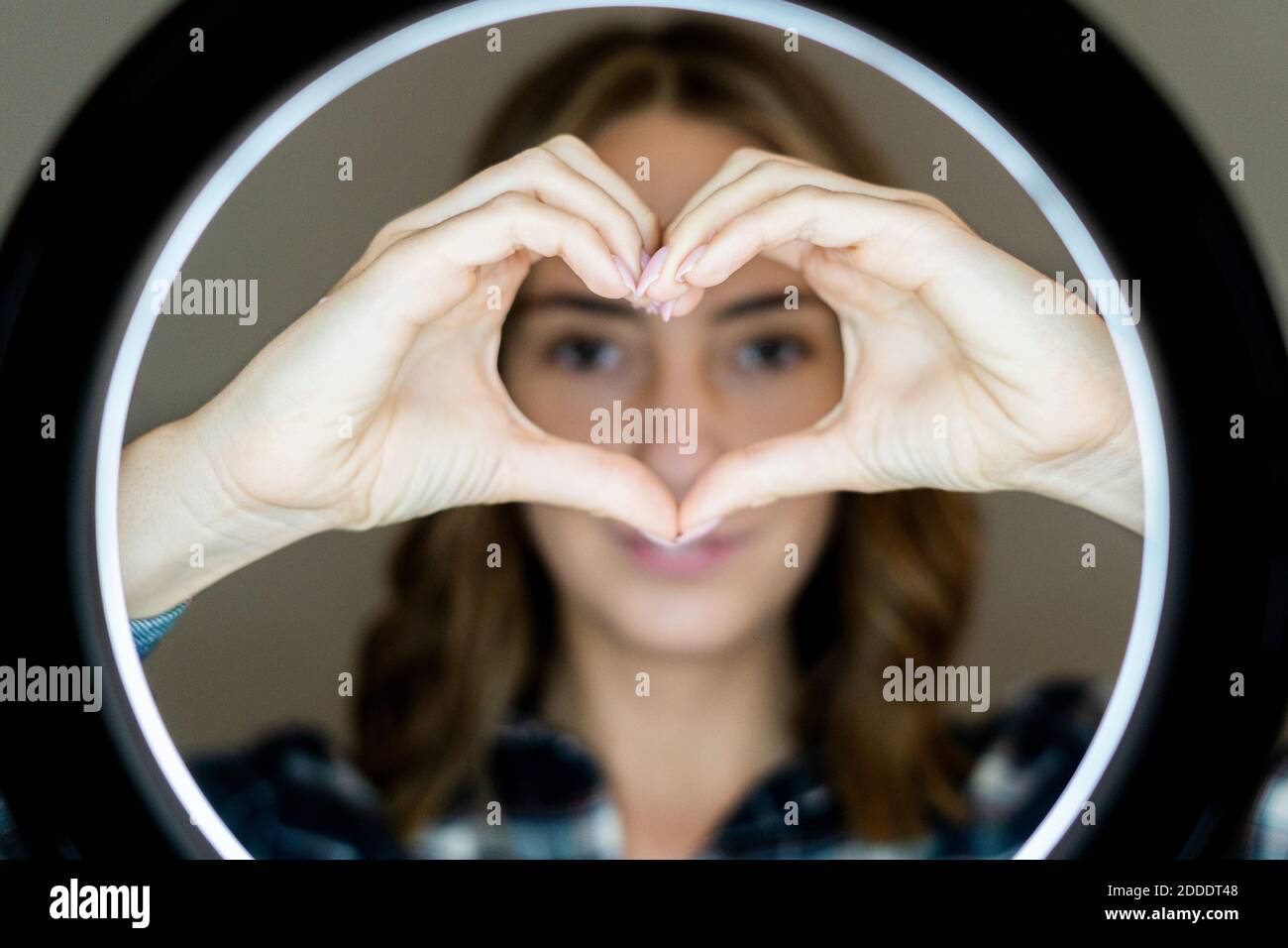 Young woman with ring flash making heart shape with hands while ...