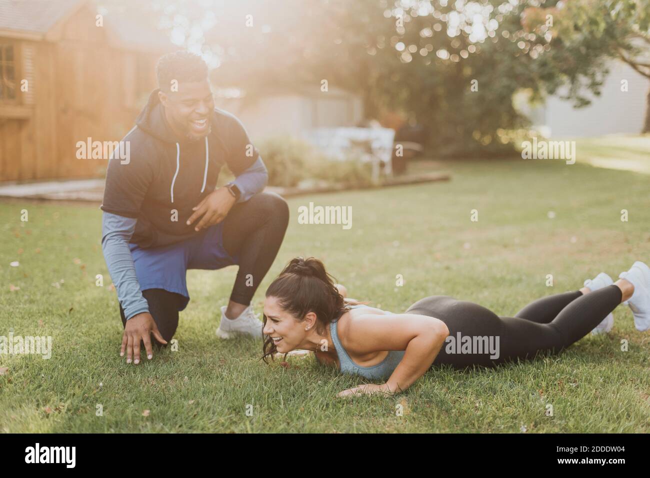 Smiling man motivating woman doing push ups at backyard Stock Photo - Alamy