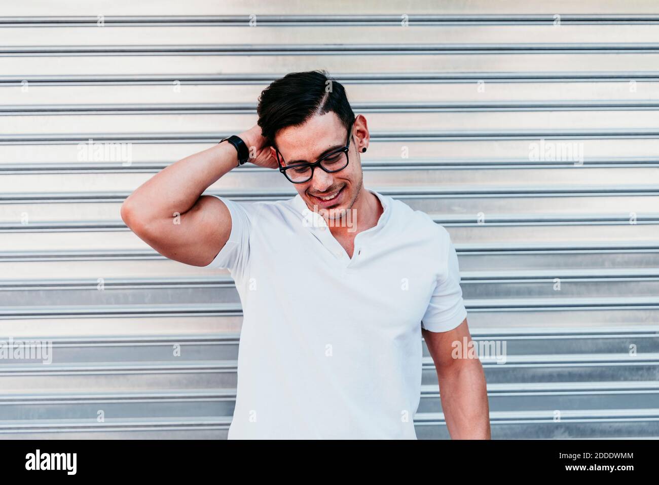 Smiling male with hand in hair standing against shutter Stock Photo - Alamy